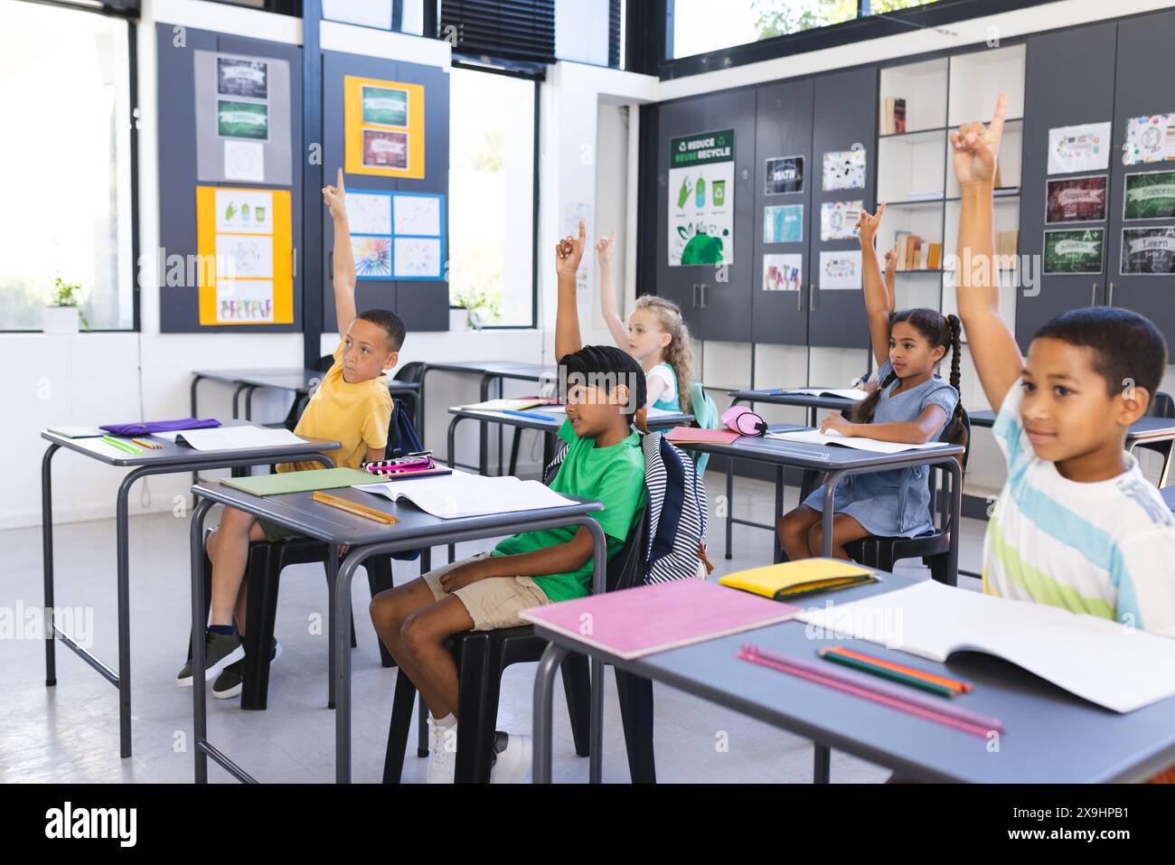 Diverse group of children raise their hands in a school classroom ...