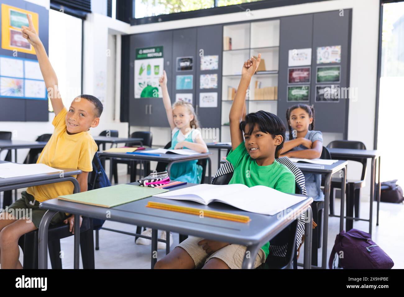 Eager children raise their hands in a bright school classroom. The ...