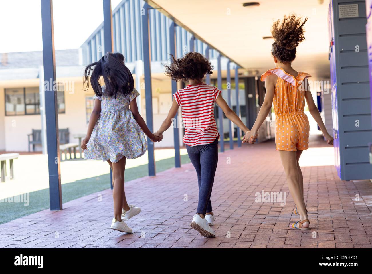 Three biracial girls walk hand in hand through a school corridor Stock ...