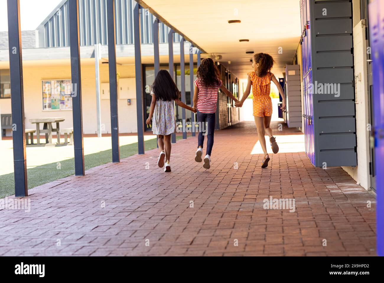 Three biracial girls are holding hands and running through a school ...