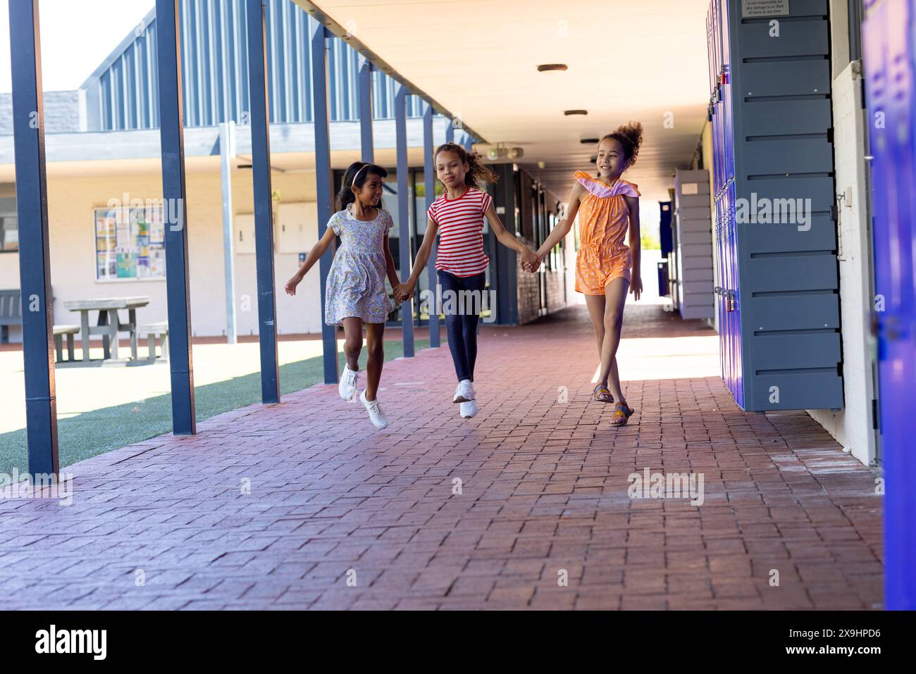 Three biracial girls are holding hands and walking through a school ...