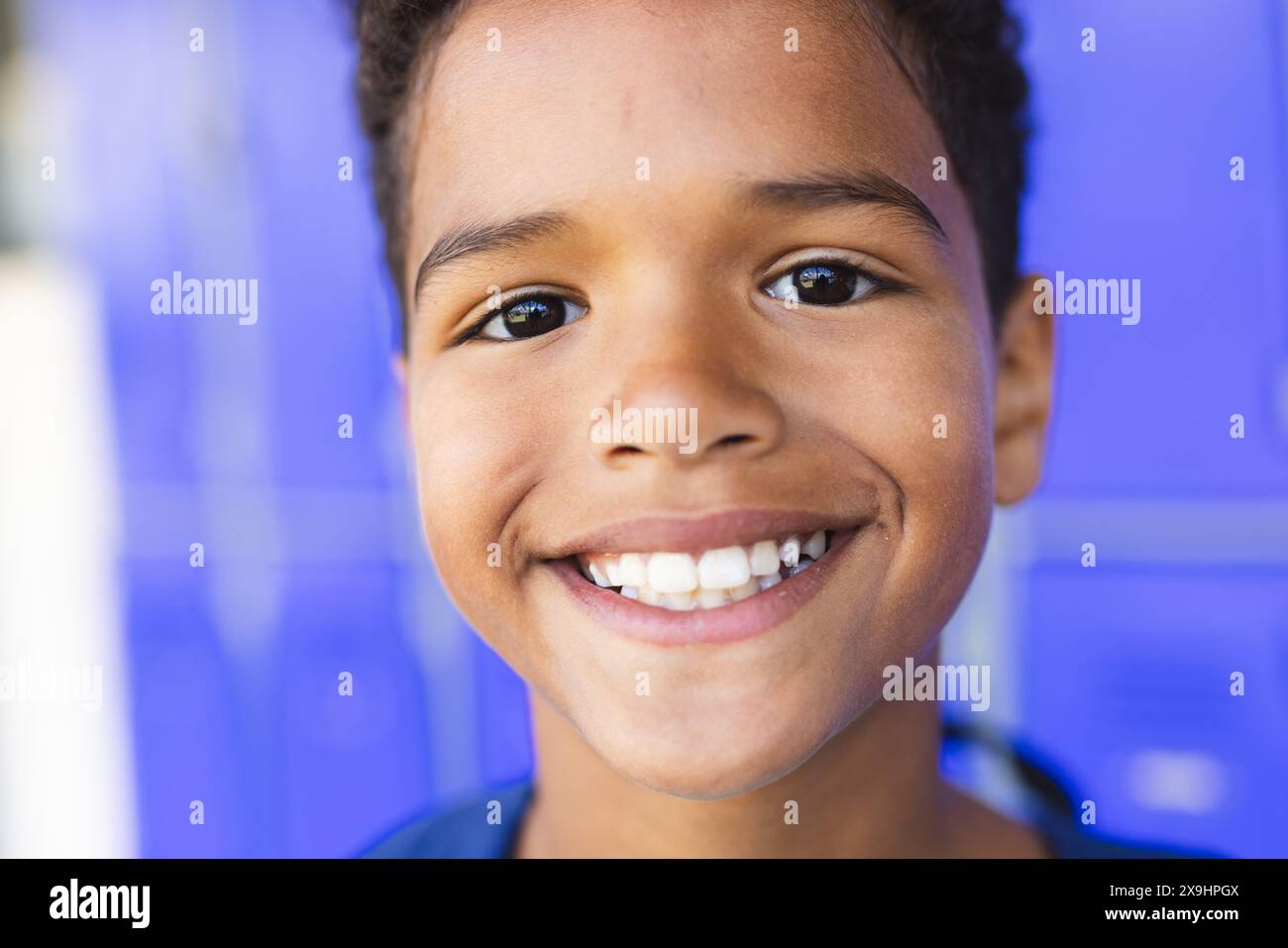 Biracial boy with a bright smile stands against a blue background in ...