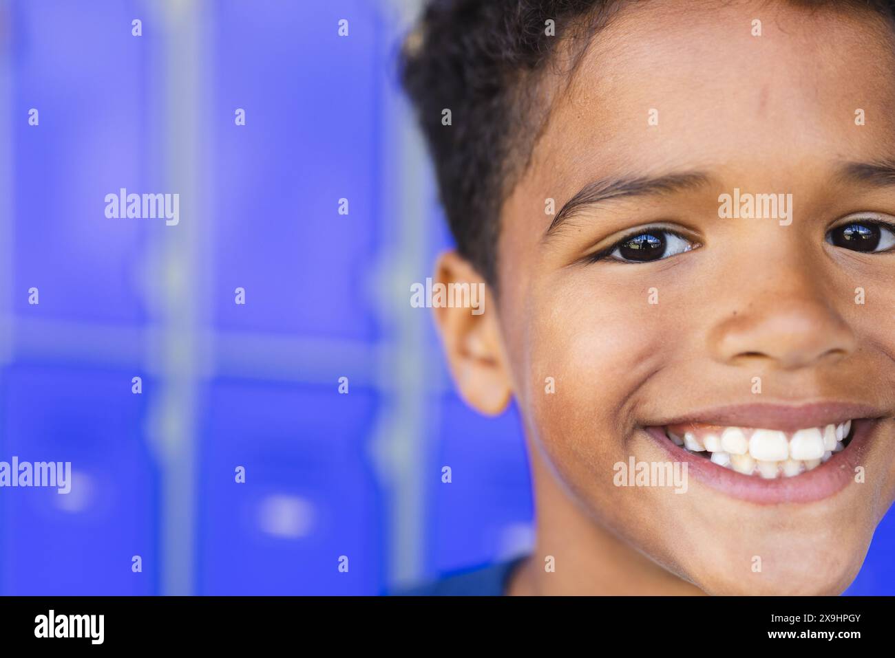 Biracial boy with a bright smile, wearing a blue shirt against a blue ...