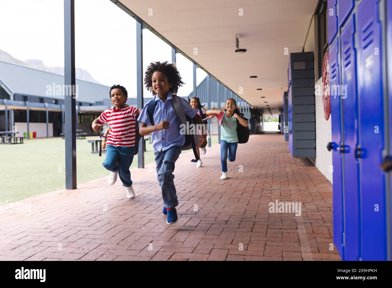 In school, diverse group of young students running in hallway outdoors ...