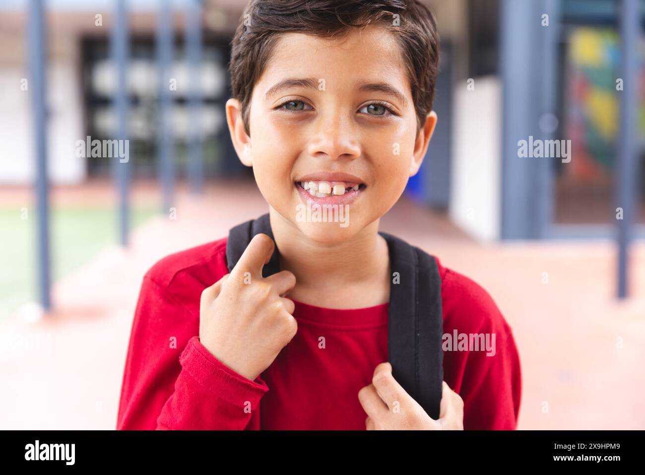 In school outdoors, biracial young boy wearing a backpack is smiling ...