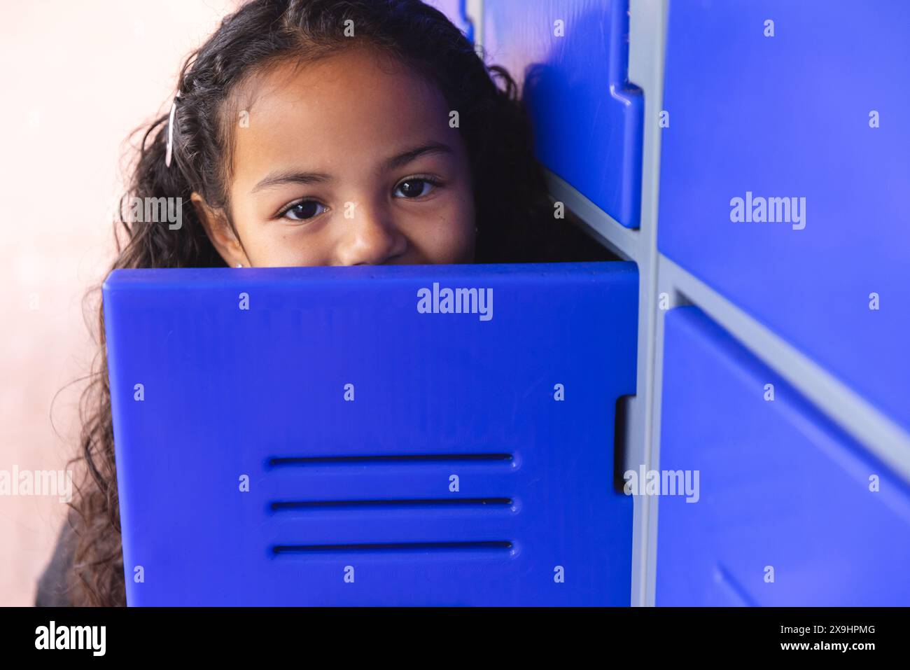 In school, young biracial girl with curly hair is peeking from behind a ...