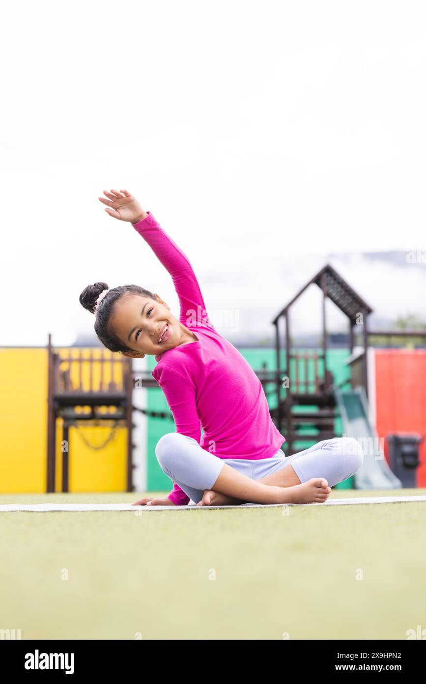 In school, young biracial girl in pink and gray stretches on playground ...