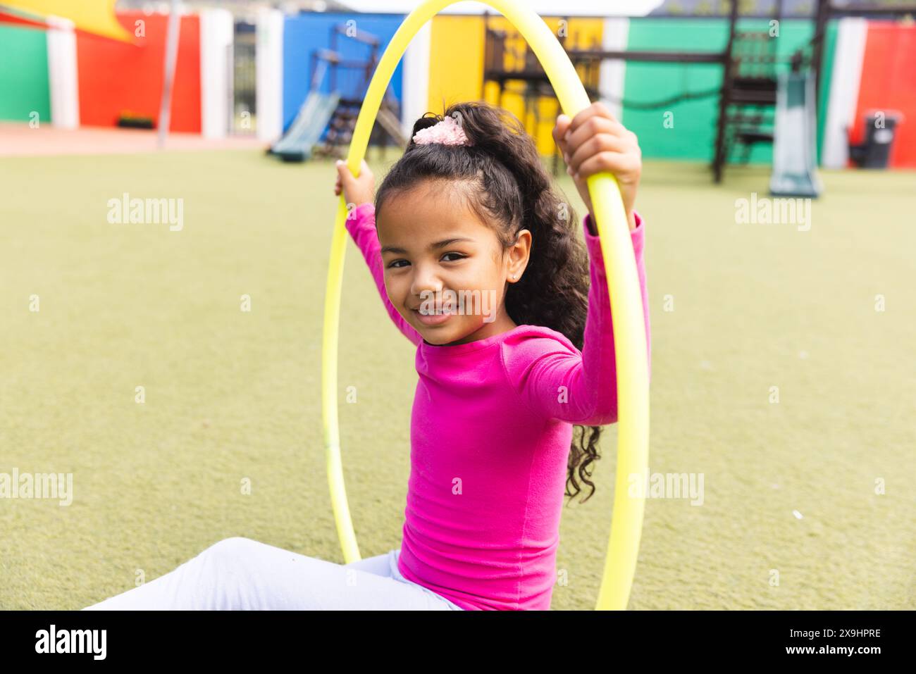 In school outdoors, biracial young girl is playing with a yellow hula ...