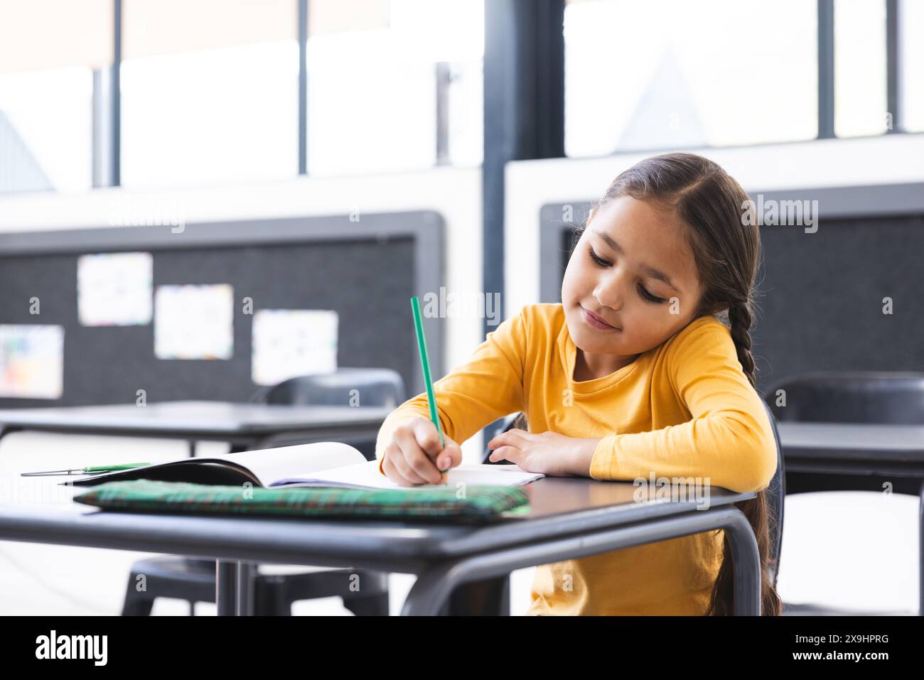 In school, in classroom, biracial young girl writing in notebook at ...