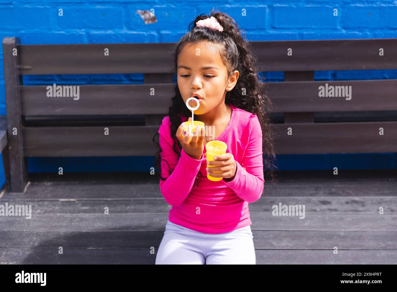 In school, young biracial girl wearing pink blowing bubbles outdoors ...