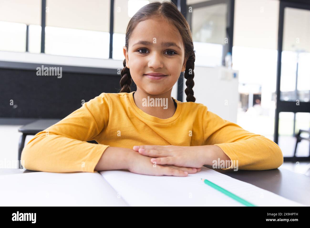 In school, biracial young girl sitting at a desk in a classroom ...