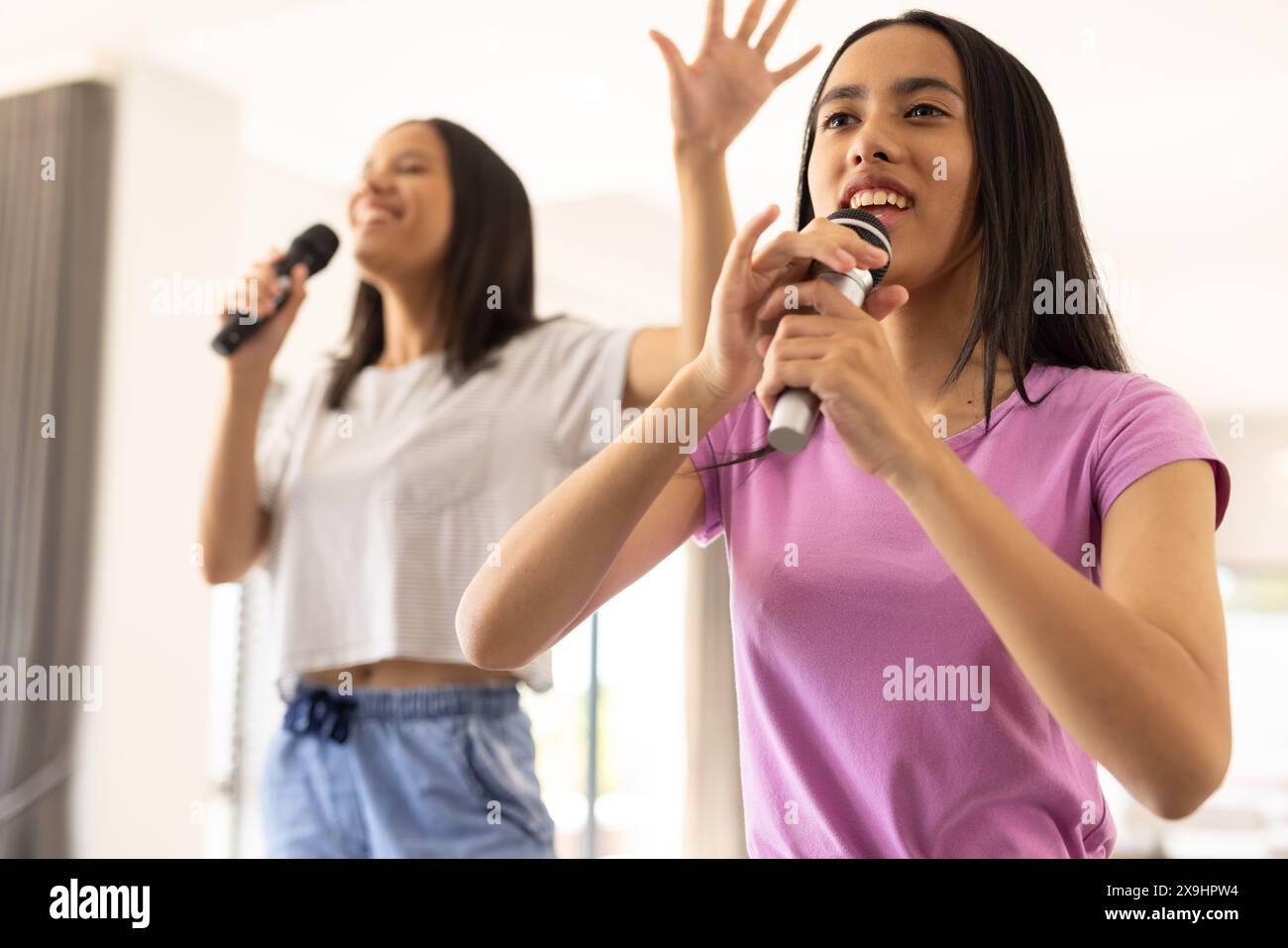 Two biracial young sisters, singing together at home, holding ...
