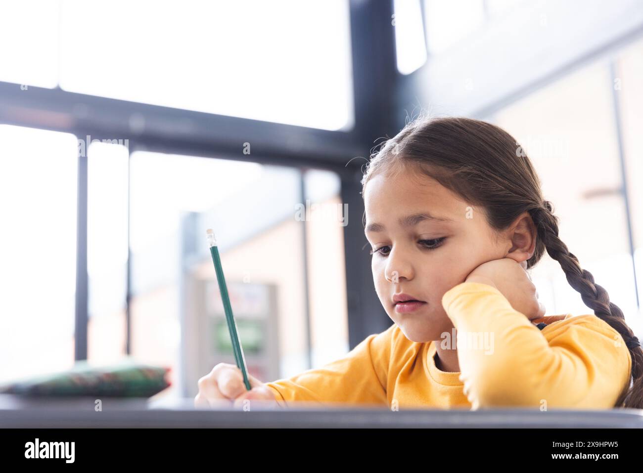 In school, in the classroom, a young biracial girl with braided hair is ...