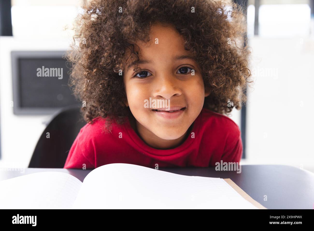 In school, young biracial male student wearing a red shirt reading a ...