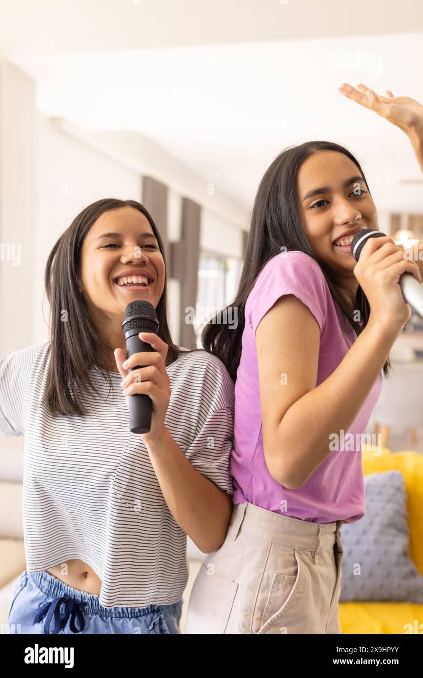 Two biracial young sisters, holding microphones at home, singing ...