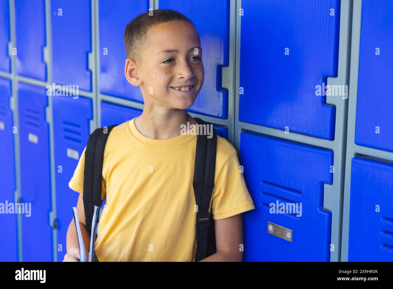 Biracial boy stands by blue lockers at school Stock Photo - Alamy