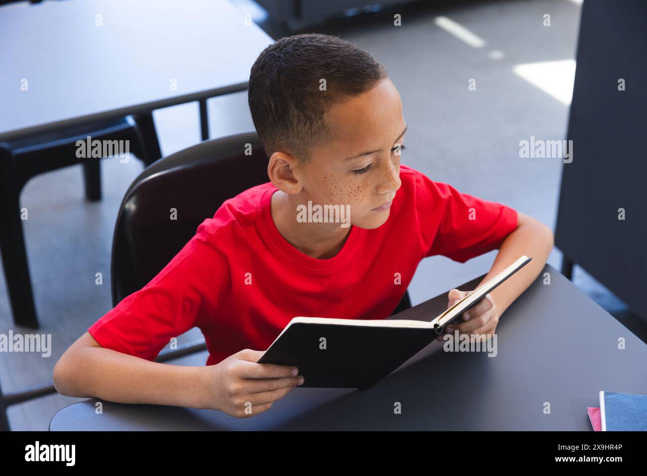 Biracial boy focused on his tablet at school Stock Photo - Alamy