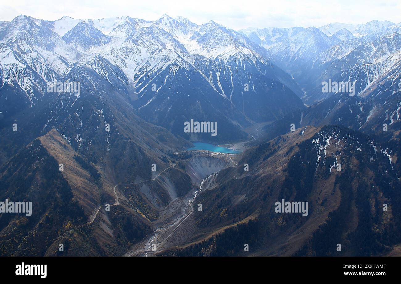 Alpine Issyk lake in a mountain gorge with snow-capped peaks and roads ...