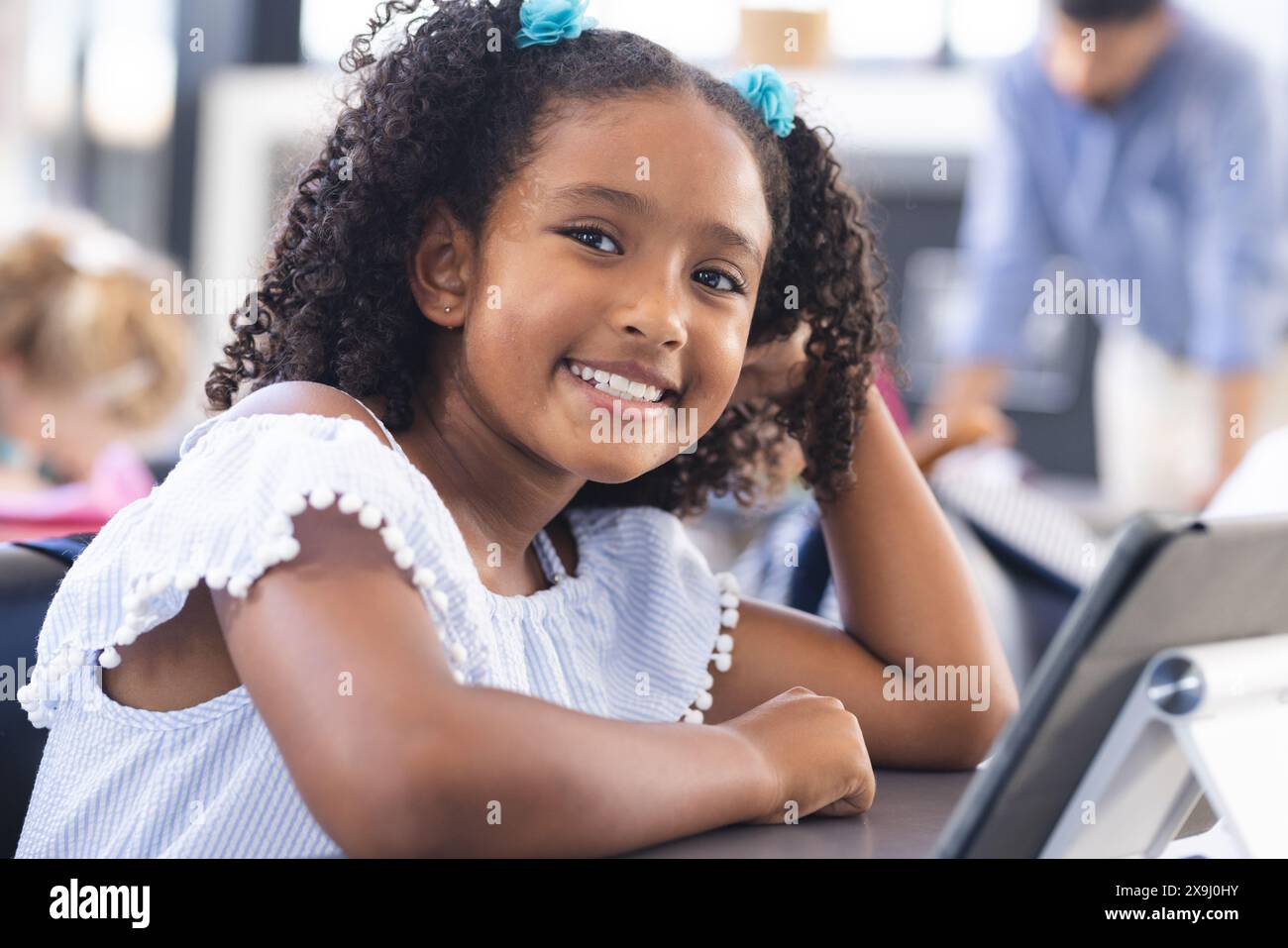 Biracial girl with curly hair and blue hair ties smiles in a school ...