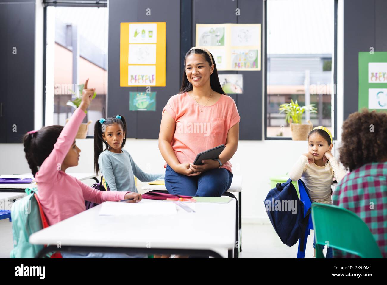 Biracial female teacher with 4 students raising their hands to ask ...