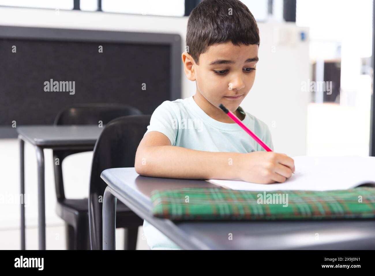 In school, young biracial boy focusing on writing in a notebook in the ...
