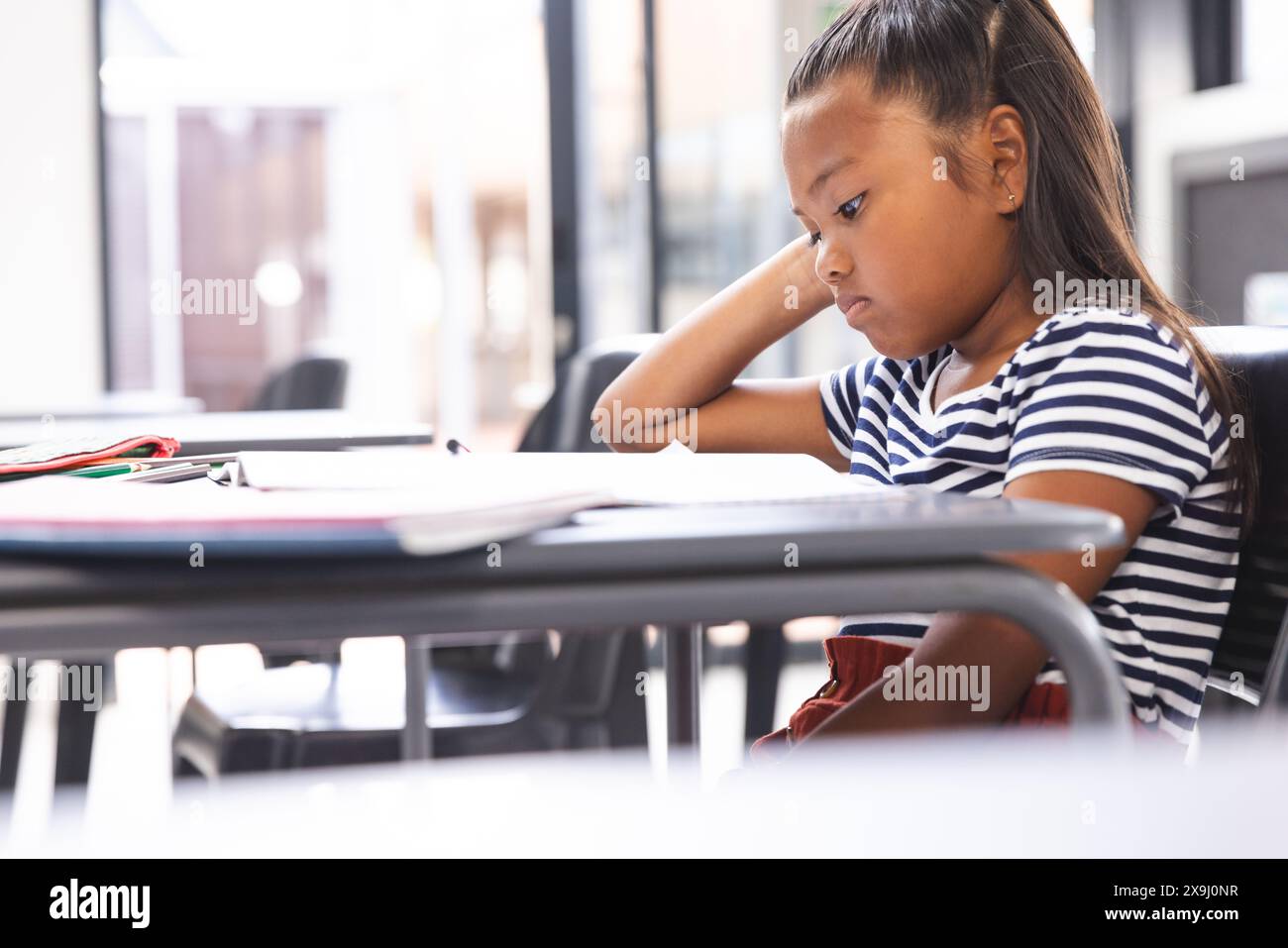 Biracial girl with long brown hair concentrates on schoolwork in class ...