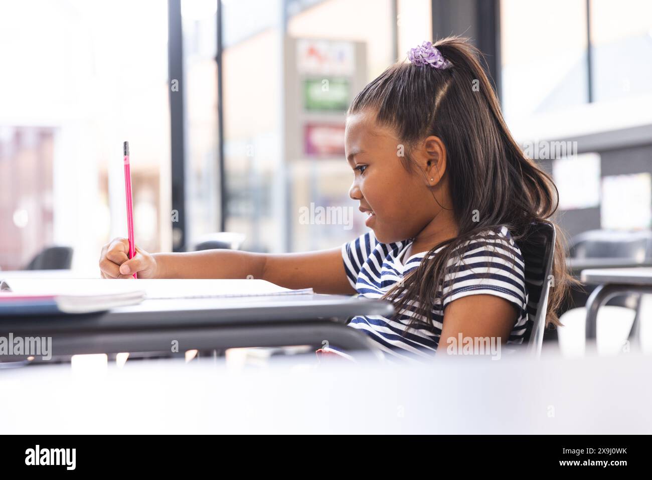 In school, young biracial girl with light brown skin is writing in the ...