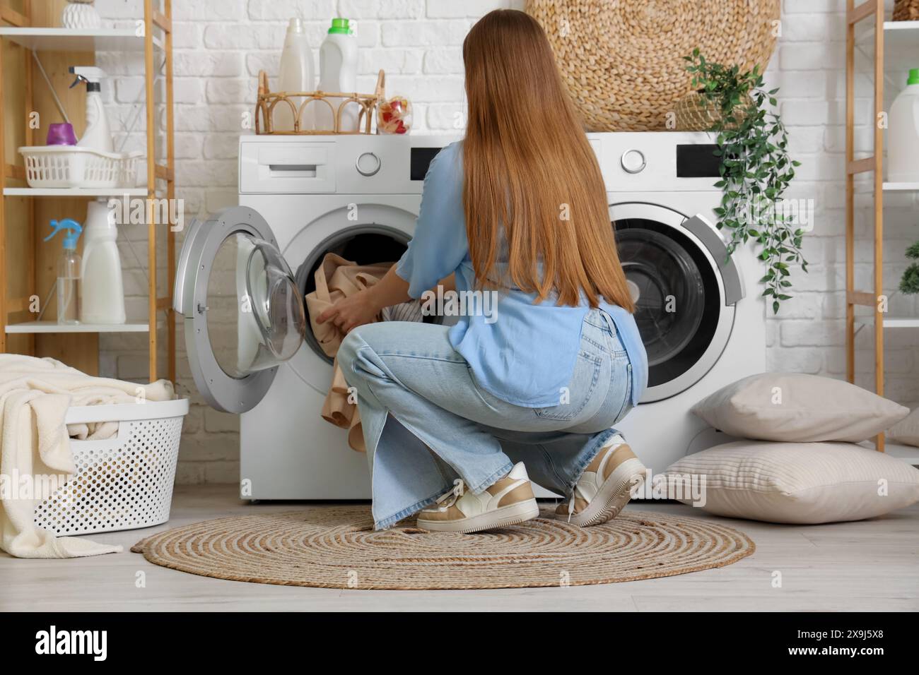 Woman putting clothes into washing machine in laundry room, back view ...