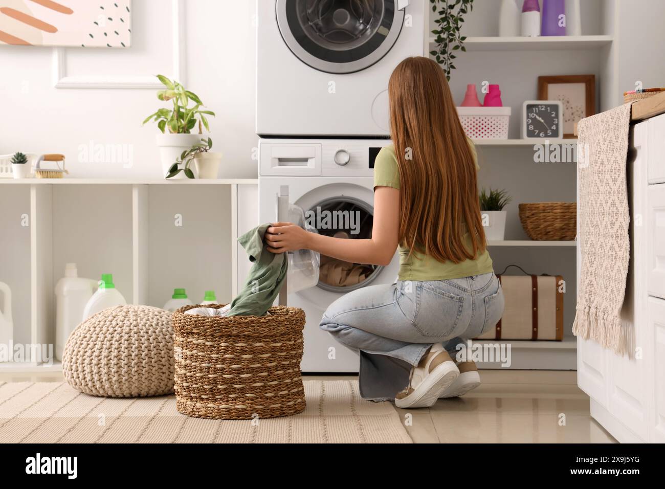 Woman with wicker basket putting clothes into washing machine in ...