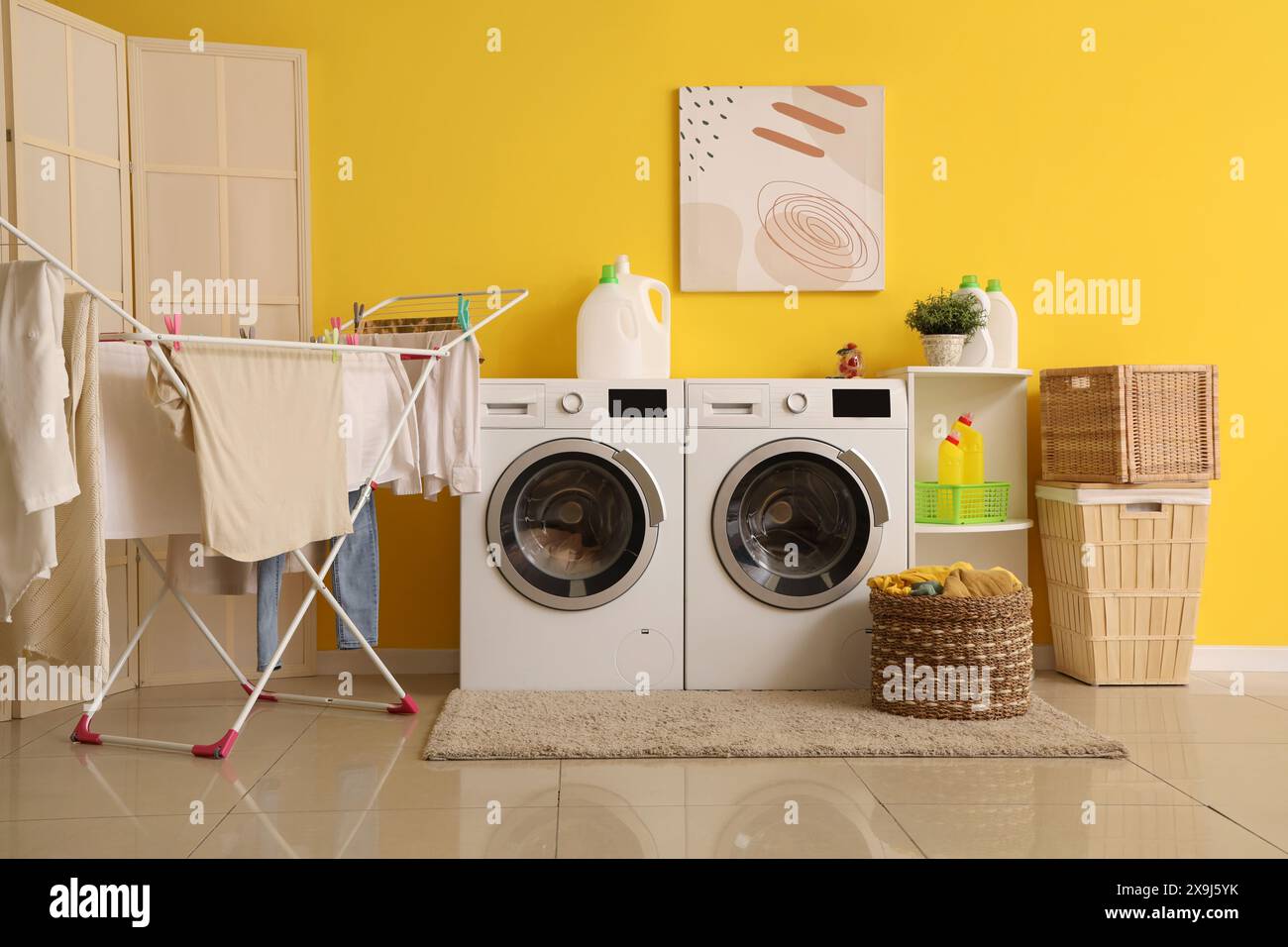Interior of modern laundry room with washing machines, clothes on dryer ...