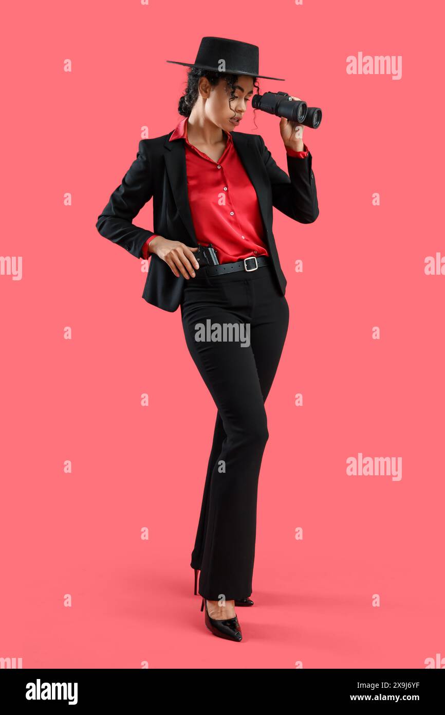 Female African-American spy with binoculars and gun on red background ...