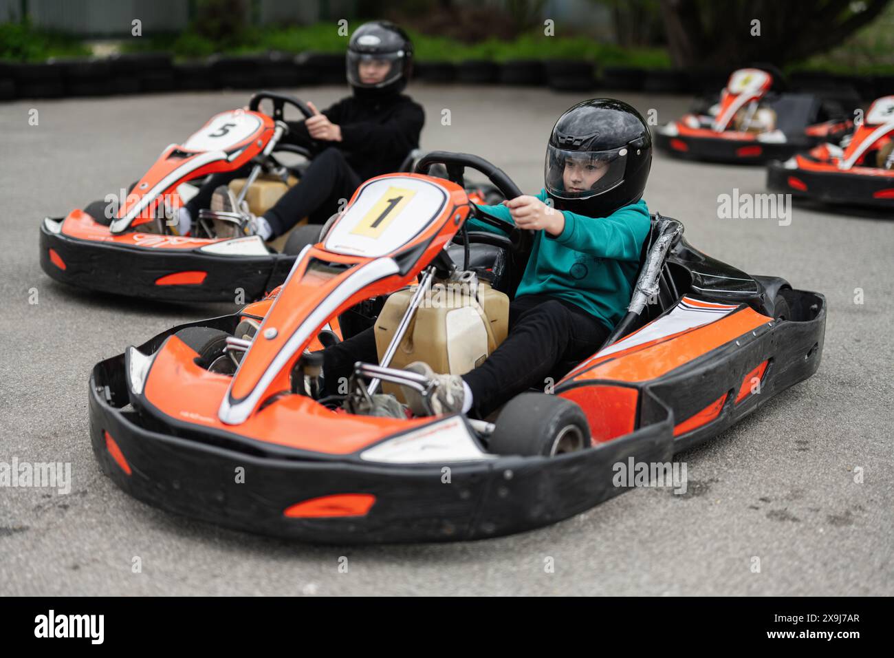 Two children in helmets racing go-karts on an outdoor track ...