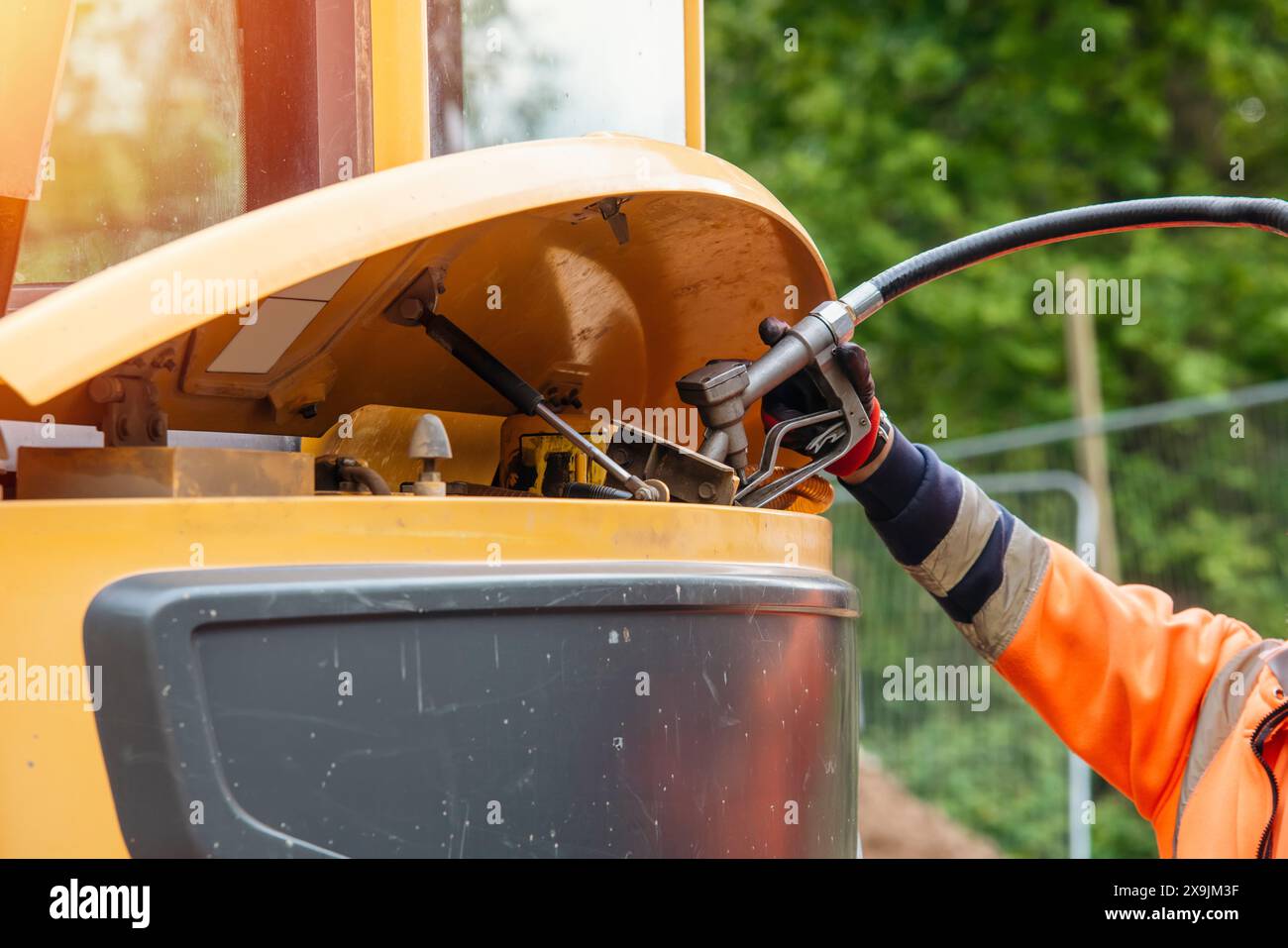 Builder in safety gloves filling excavator with diesel fuel on building ...