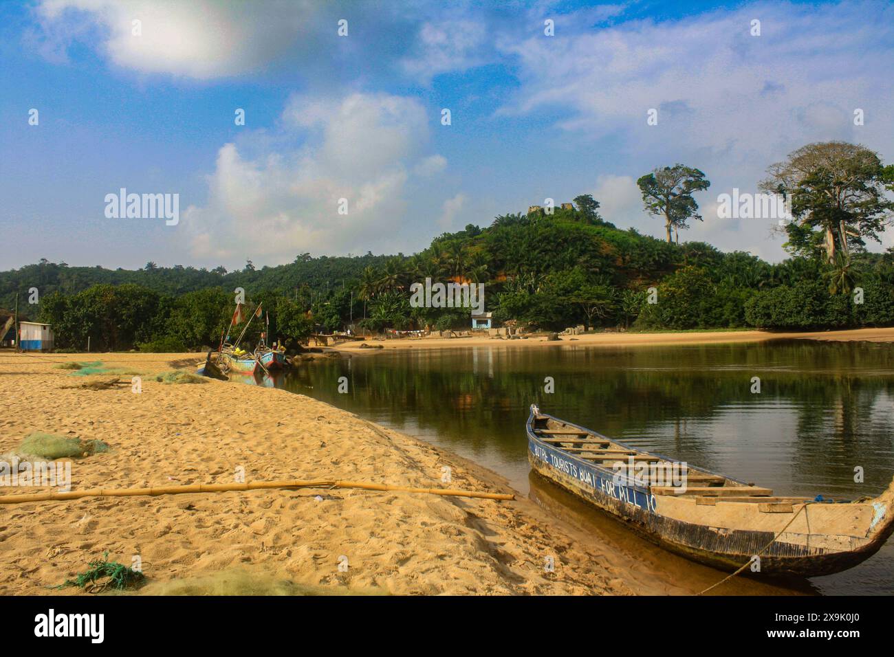 A peaceful scene of a river beach with traditional fishing boats, lush ...
