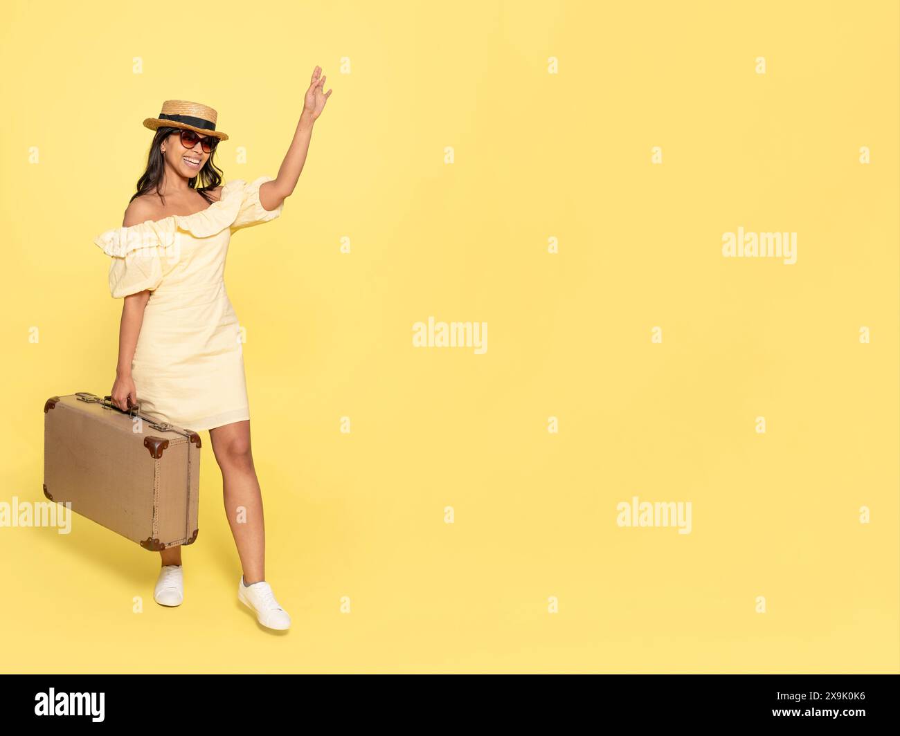 a woman inyellow dress and hat, carrying a suitcase and taking photos ...