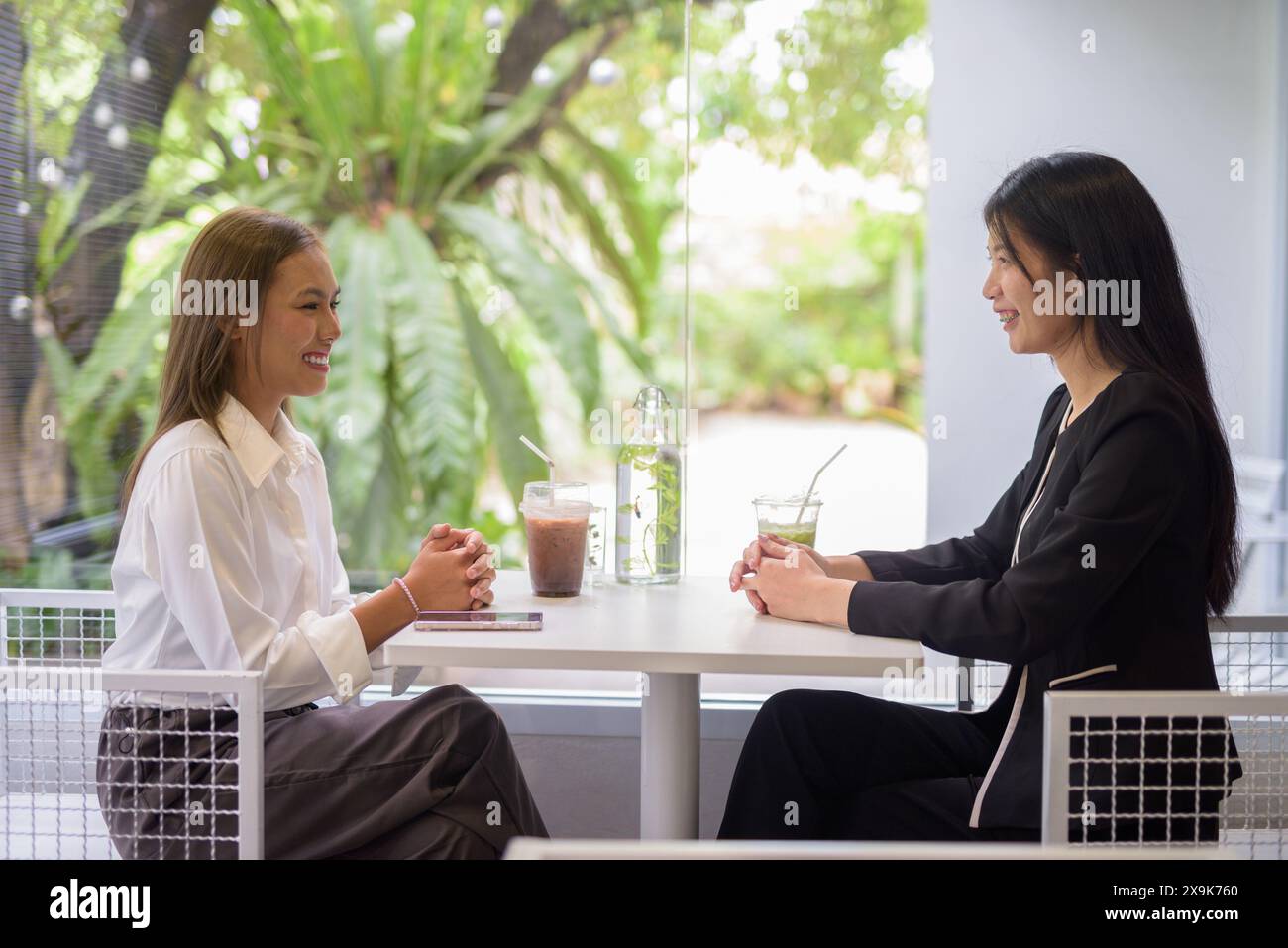 Two Asian women having a pleasant conversation over coffee in a modern ...