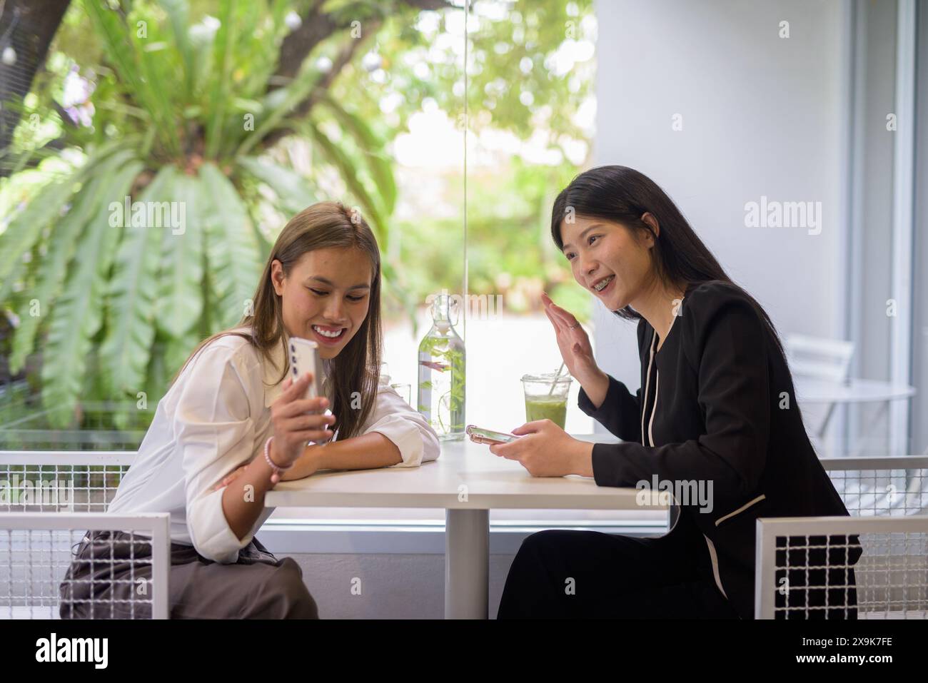 Two Asian women having a pleasant conversation over coffee in a modern ...