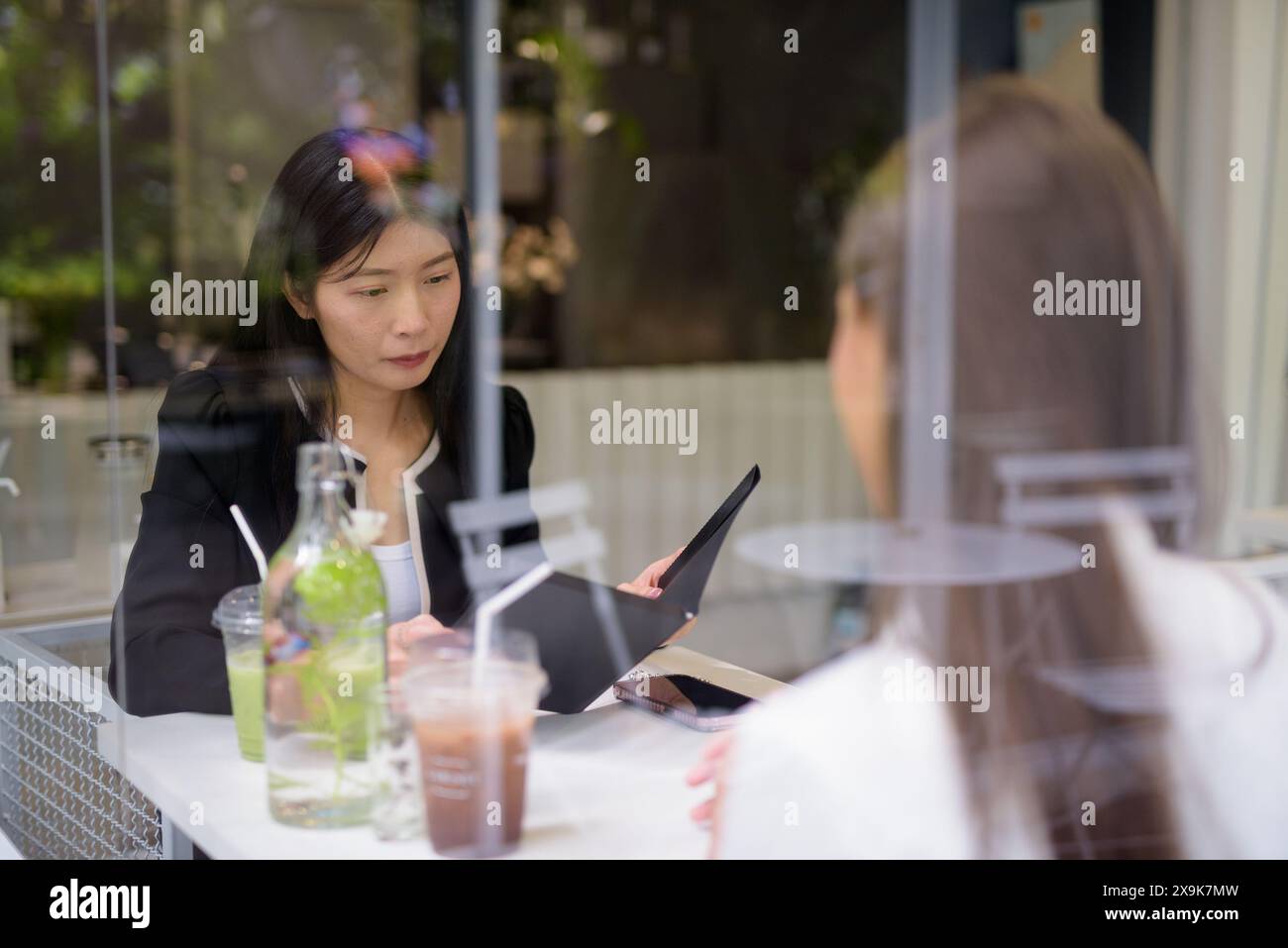 Two Asian women having a pleasant conversation over coffee in a modern ...