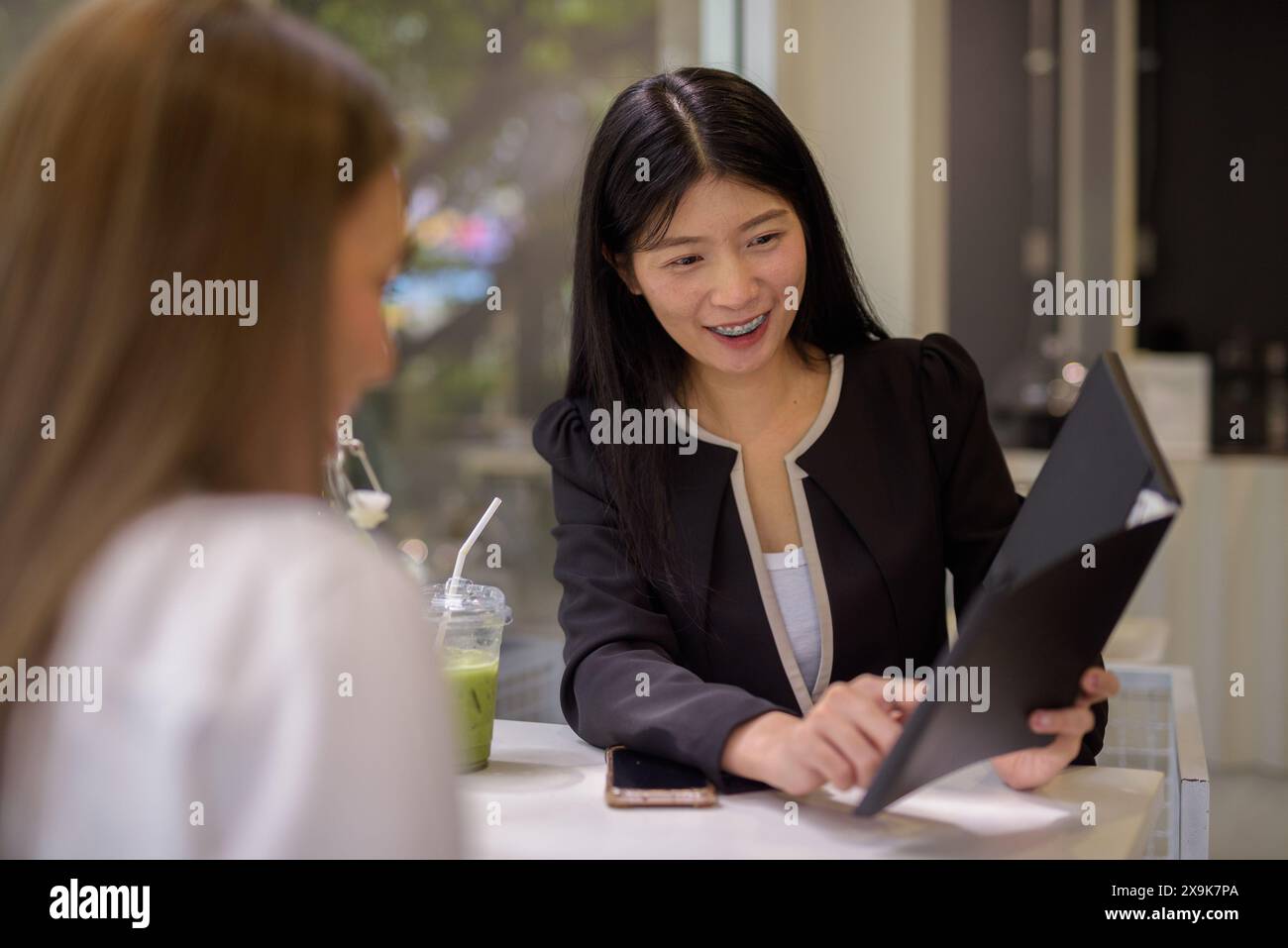 Two Asian women having a pleasant conversation over coffee in a modern ...