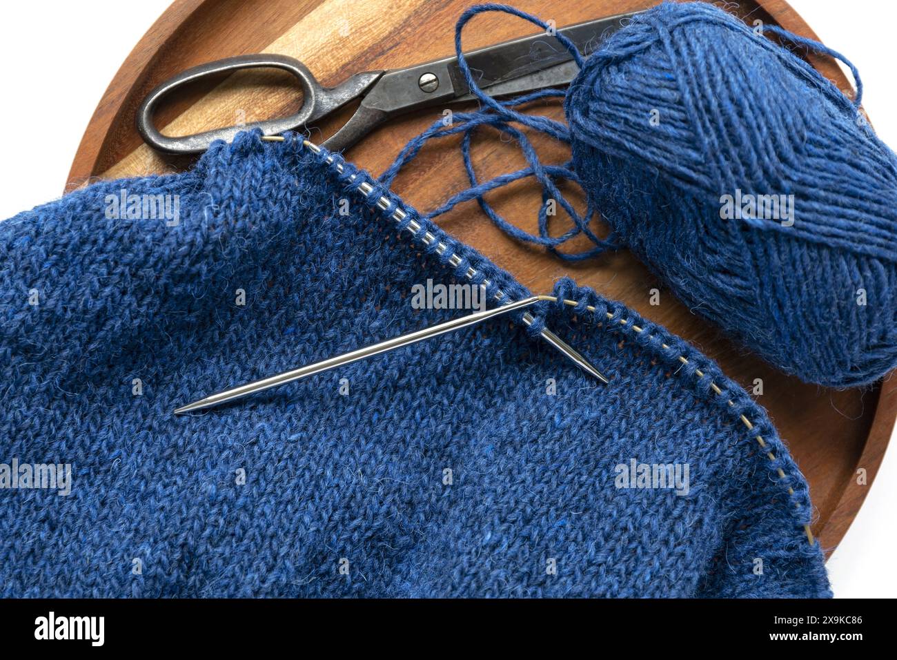 Flat lay photography of a blue wool yarn knitting on the metal needles ...