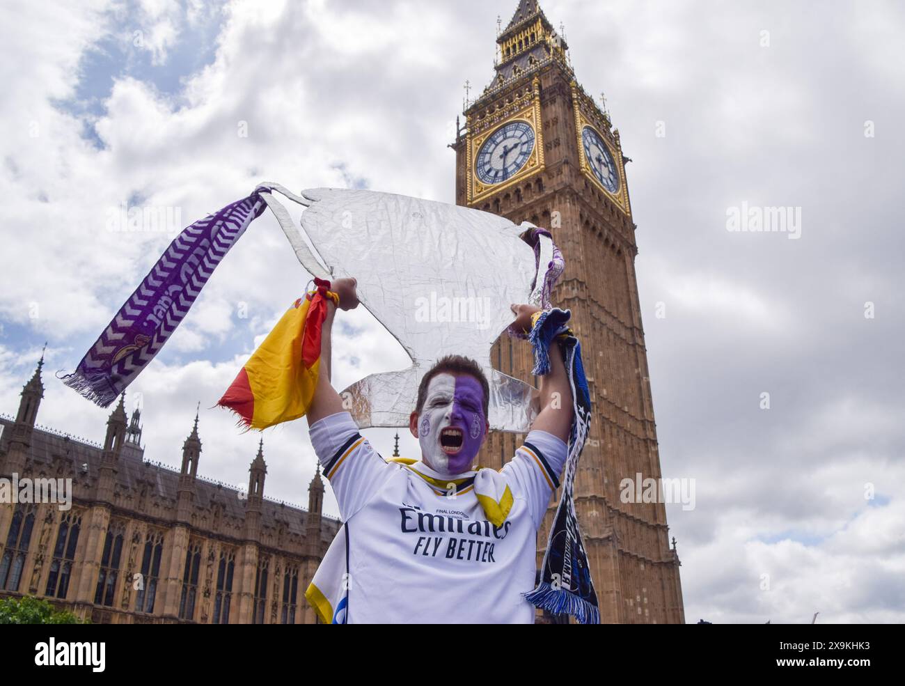 A Real Madrid fan with a painted face holds a large cardboard trophy ...