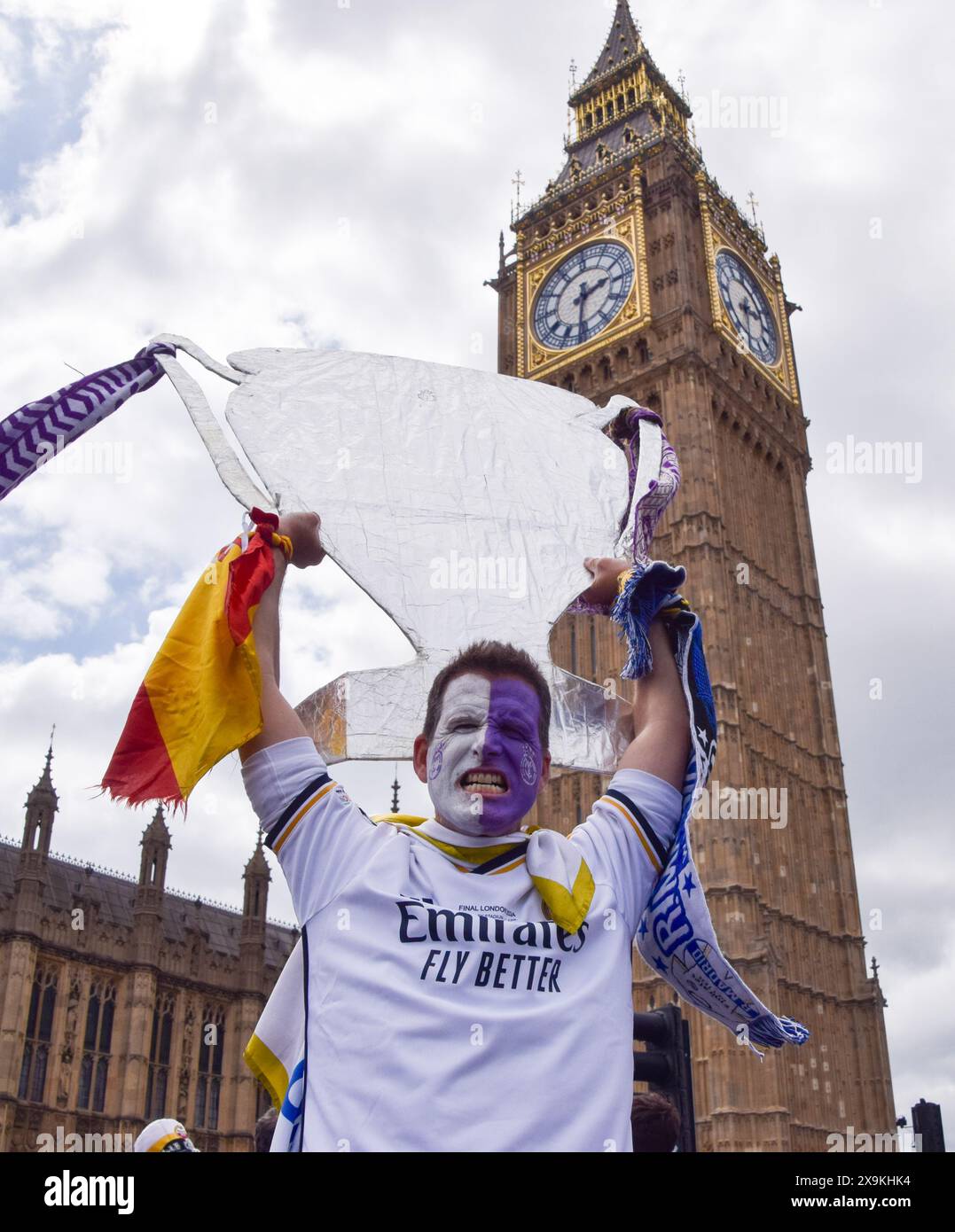 A Real Madrid fan with a painted face holds a large cardboard trophy ...