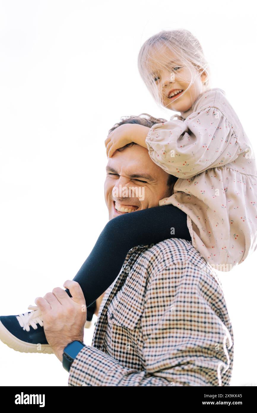 Little laughing girl hugs her smiling father head while sitting on his ...