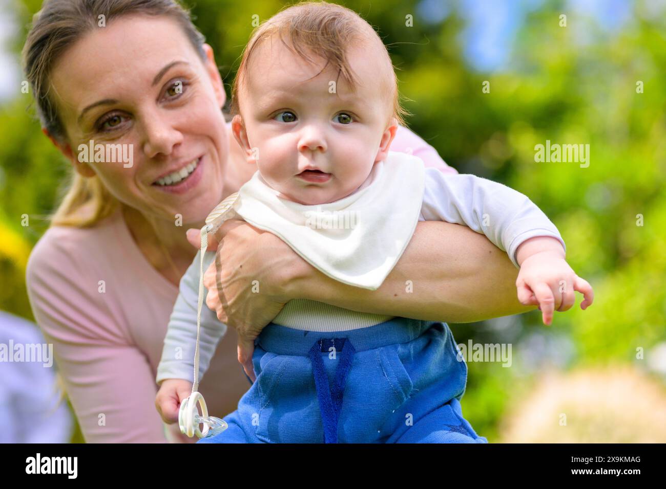A happy mother, dressed in pink, holds her baby, who wears a white bib ...