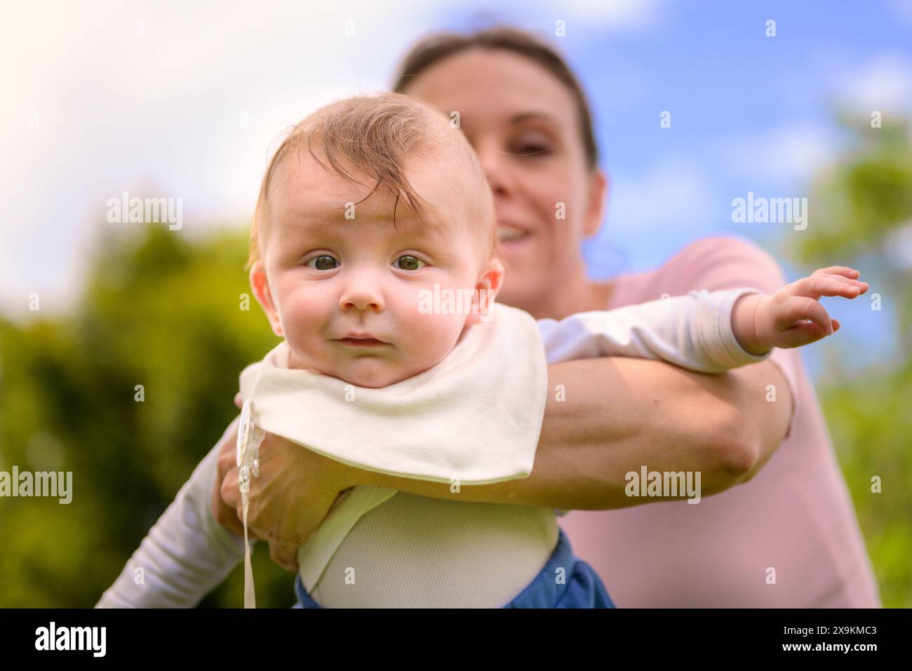 A mother joyfully holds her baby up in the air, with the baby looking ...