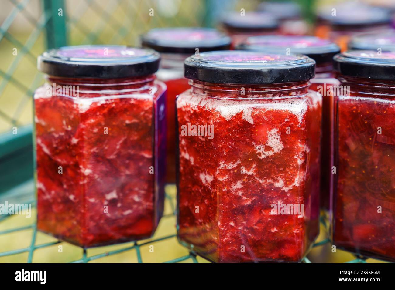 Fresh strawberry jam, preserved in jars, stands in a mesh metal box ...