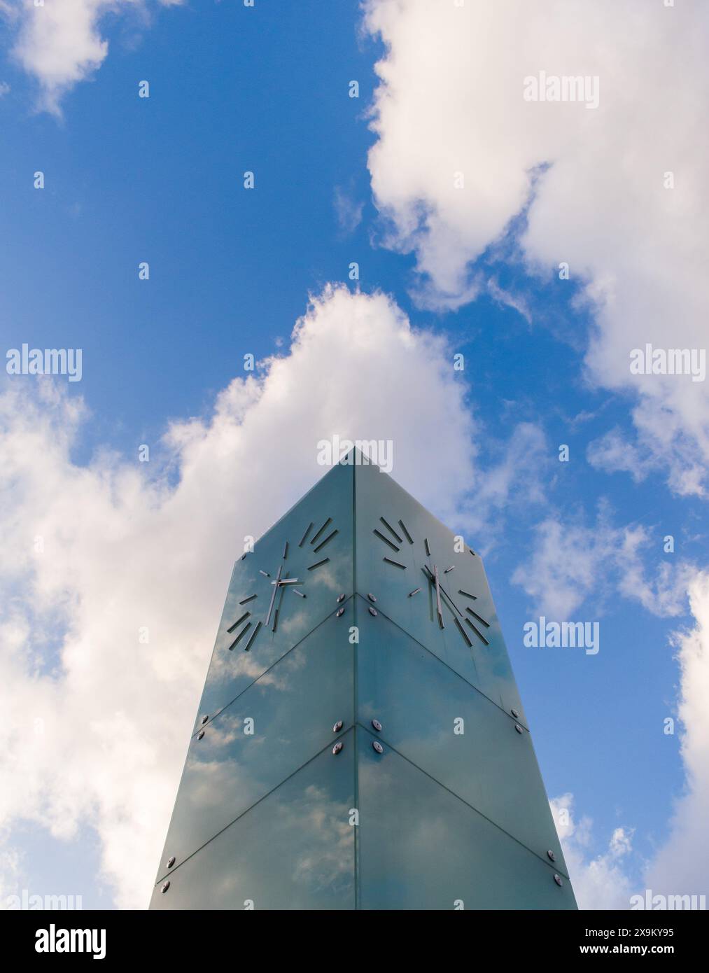 Upward view of a modern clock tower against a blue sky with clouds ...