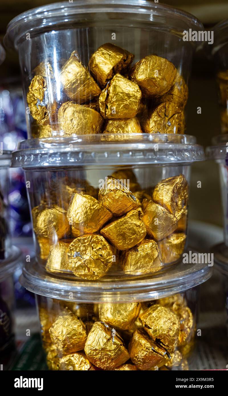Three transparent containers overflow with golden wrapped chocolates ...