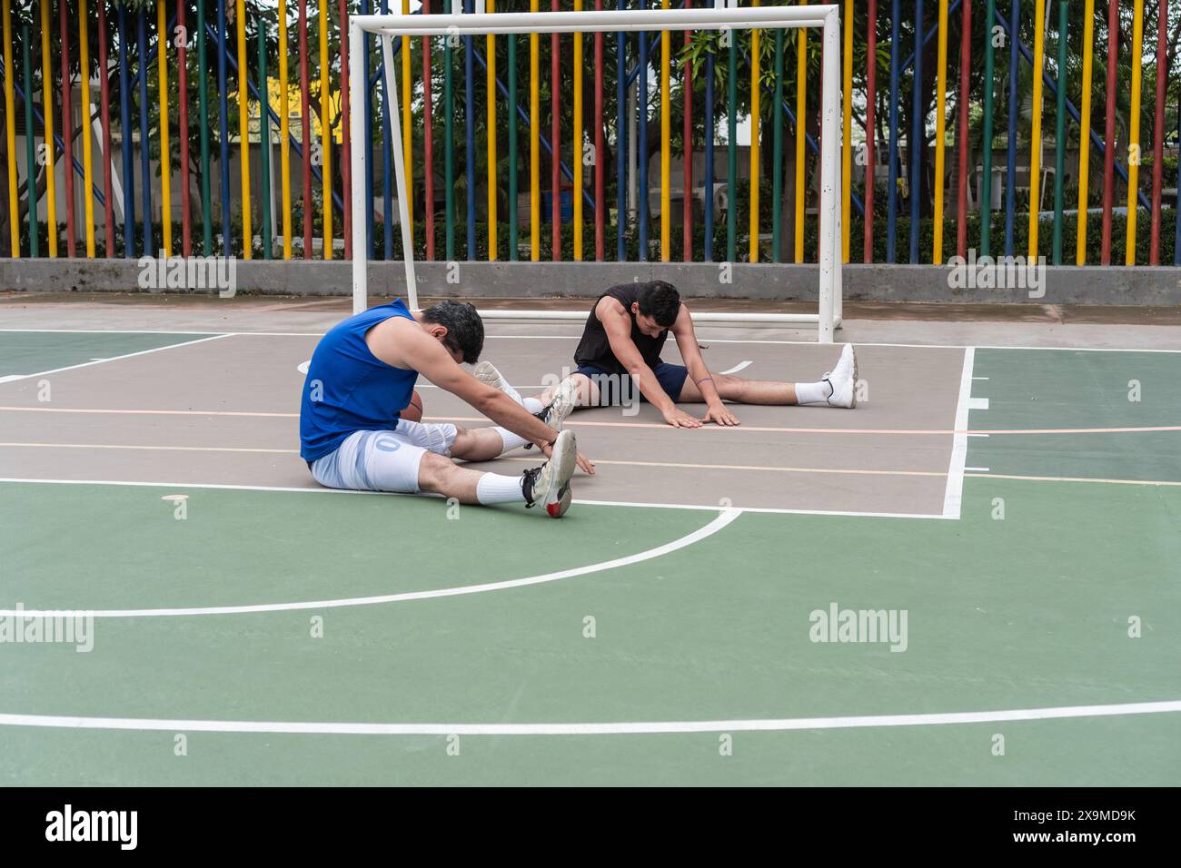 Two men wearing athletic gear stretch on an outdoor basketball court ...