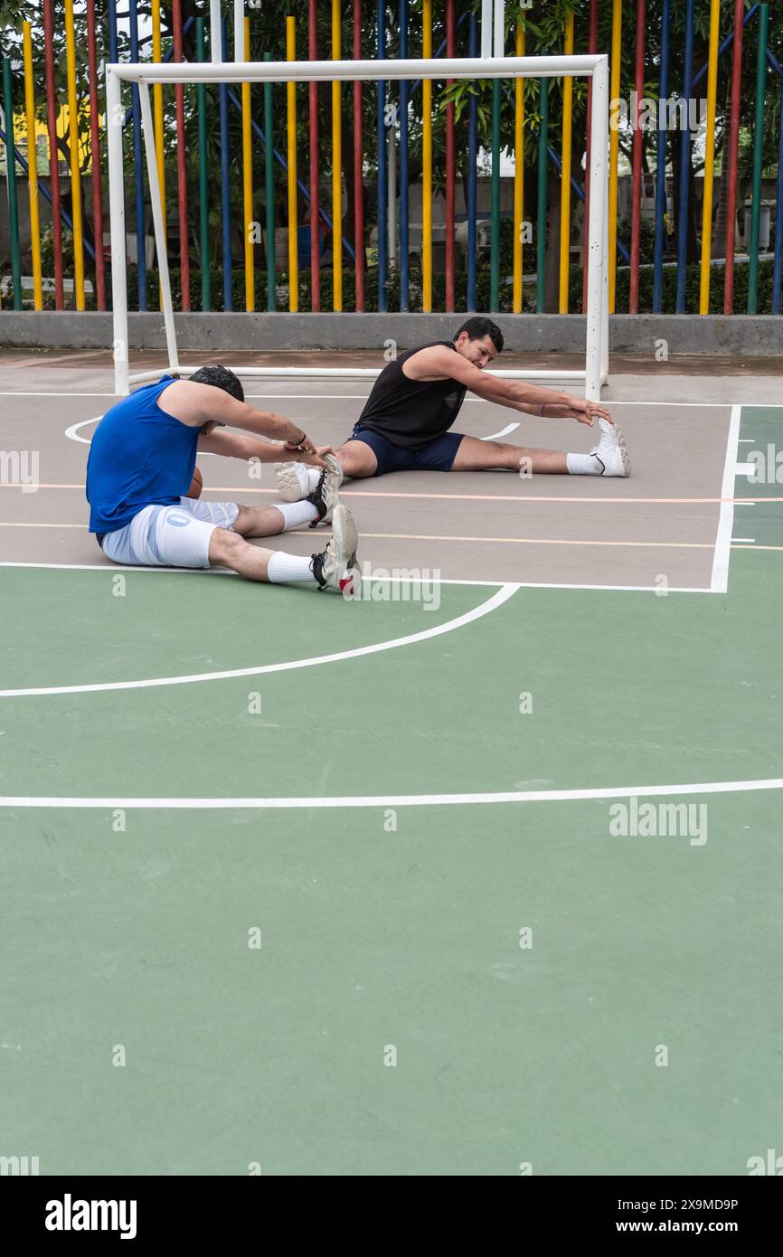 Two male athletes in sportswear stretch on an outdoor basketball court ...
